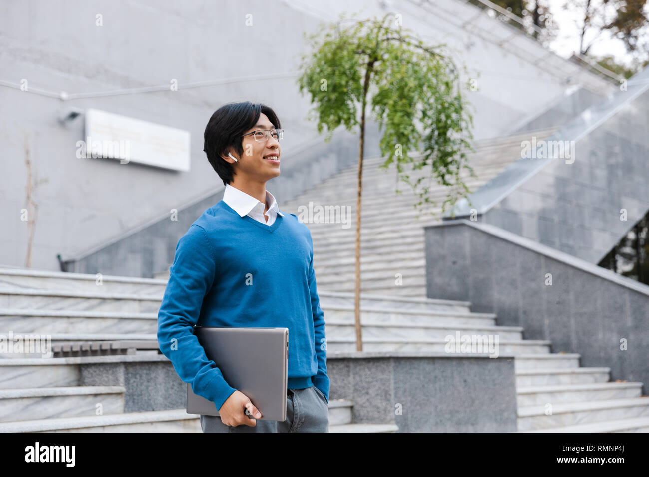 Smiling asian business man carrying laptop computer outdoors, walking ...