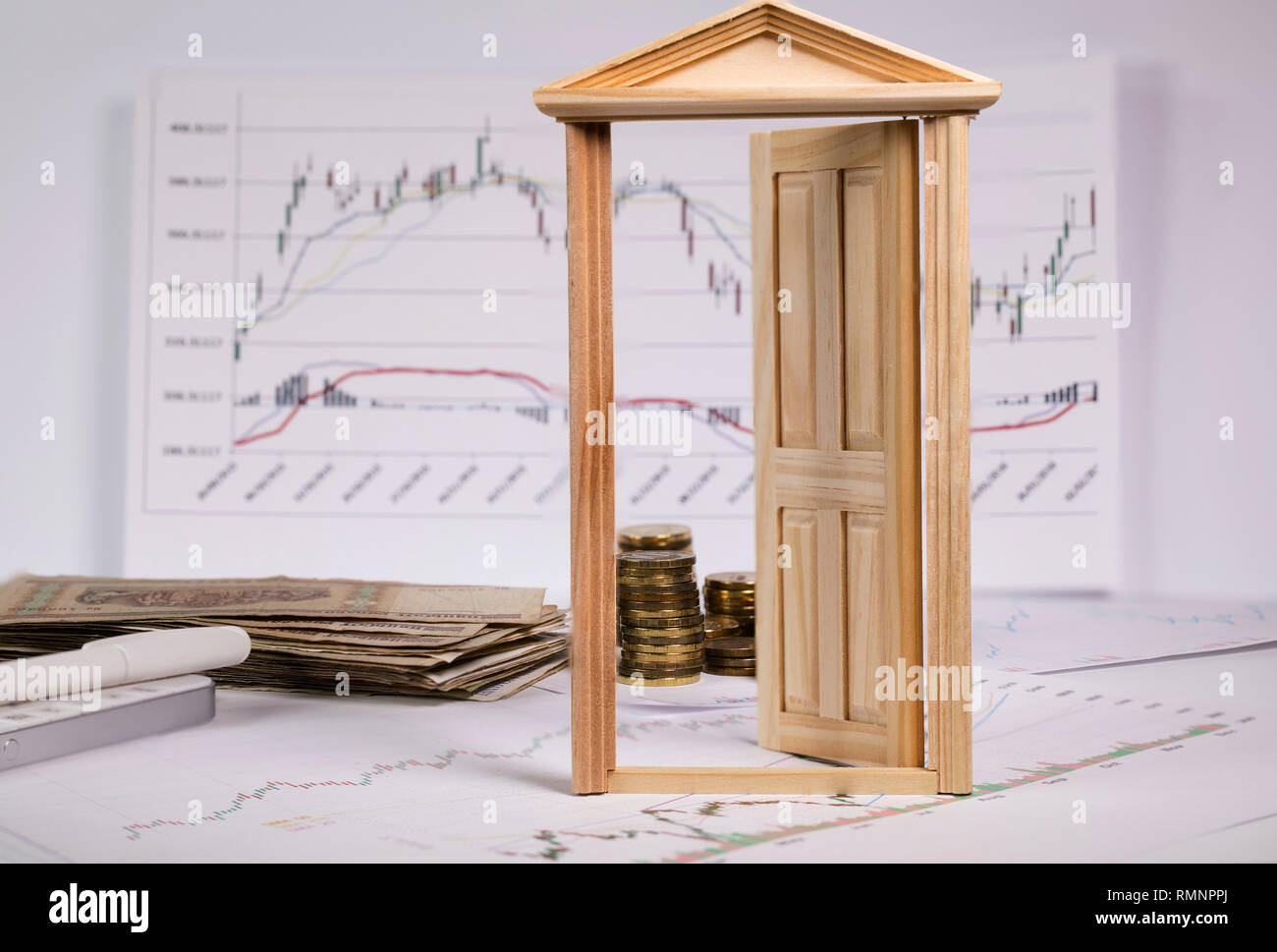 Coins on a stock market charts behind opened small wooden door. Closeup ...