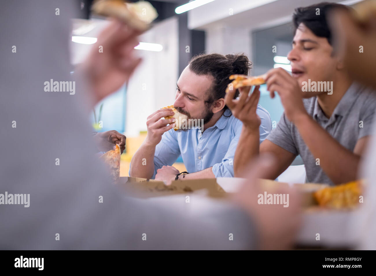 Friendly diverse multiethnic business team eating sharing pizza together in startup office ...