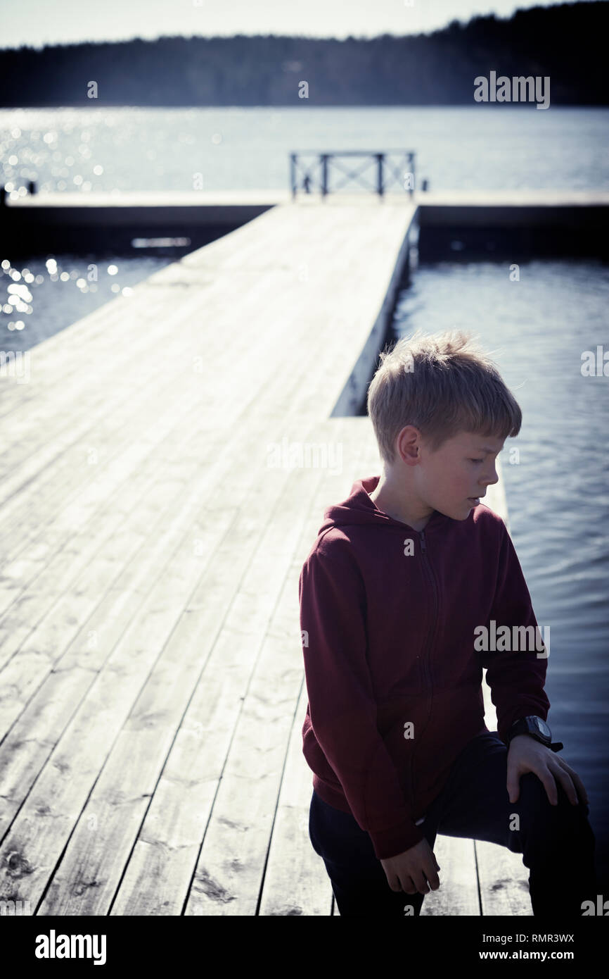 Boy sitting on jetty Stock Photo - Alamy