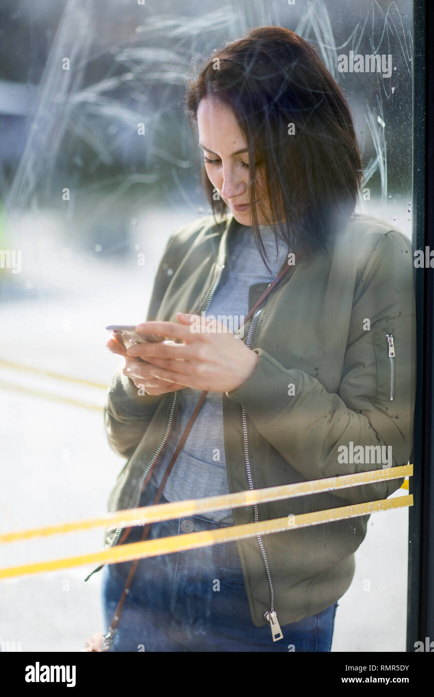Woman on bus stop using cell phone Stock Photo - Alamy