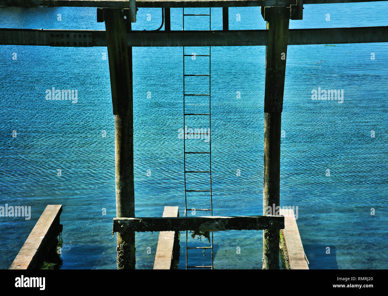 Wooden dock pillars and ladder with blue water in the background Stock ...