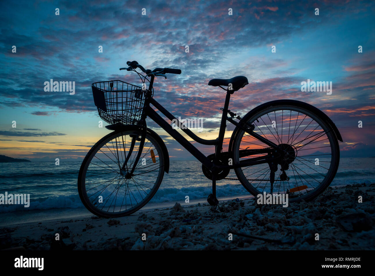 Silhouette of vintage bicycle with a basket on the beach in the evening ...