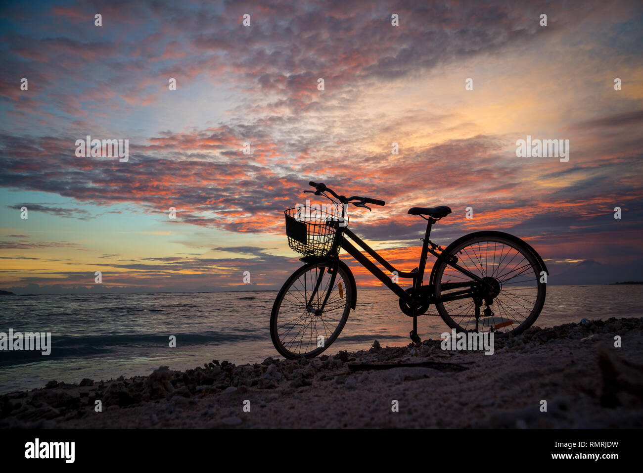 Silhouette of vintage bicycle with a basket on the beach in the evening ...