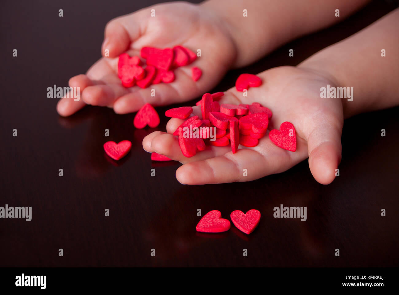 Child's hands holding red hearts on black background Stock Photo - Alamy