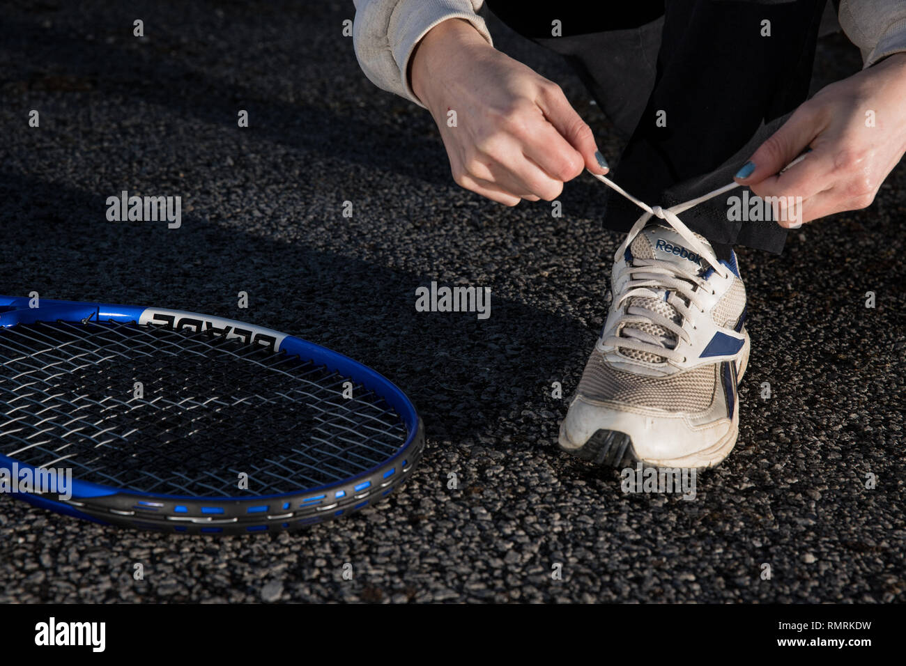 Tennis racket on the ground next to lady kneeling down tying her tennis ...