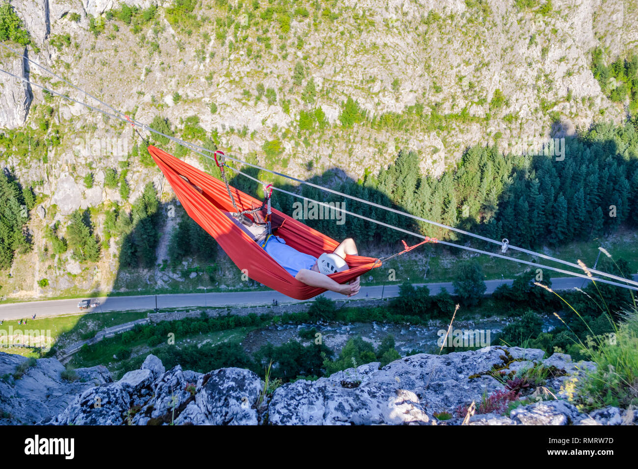 Man relaxing on a hammock set up high on a steel wire, between rock ...