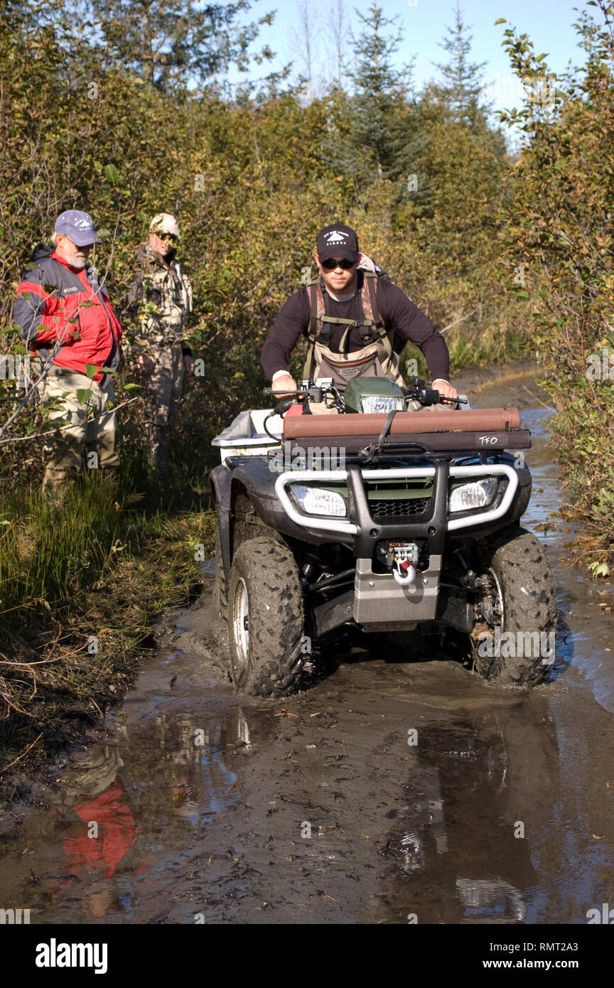 Fishing guide driving an ATV on a very muddy access road near Icy Bay ...