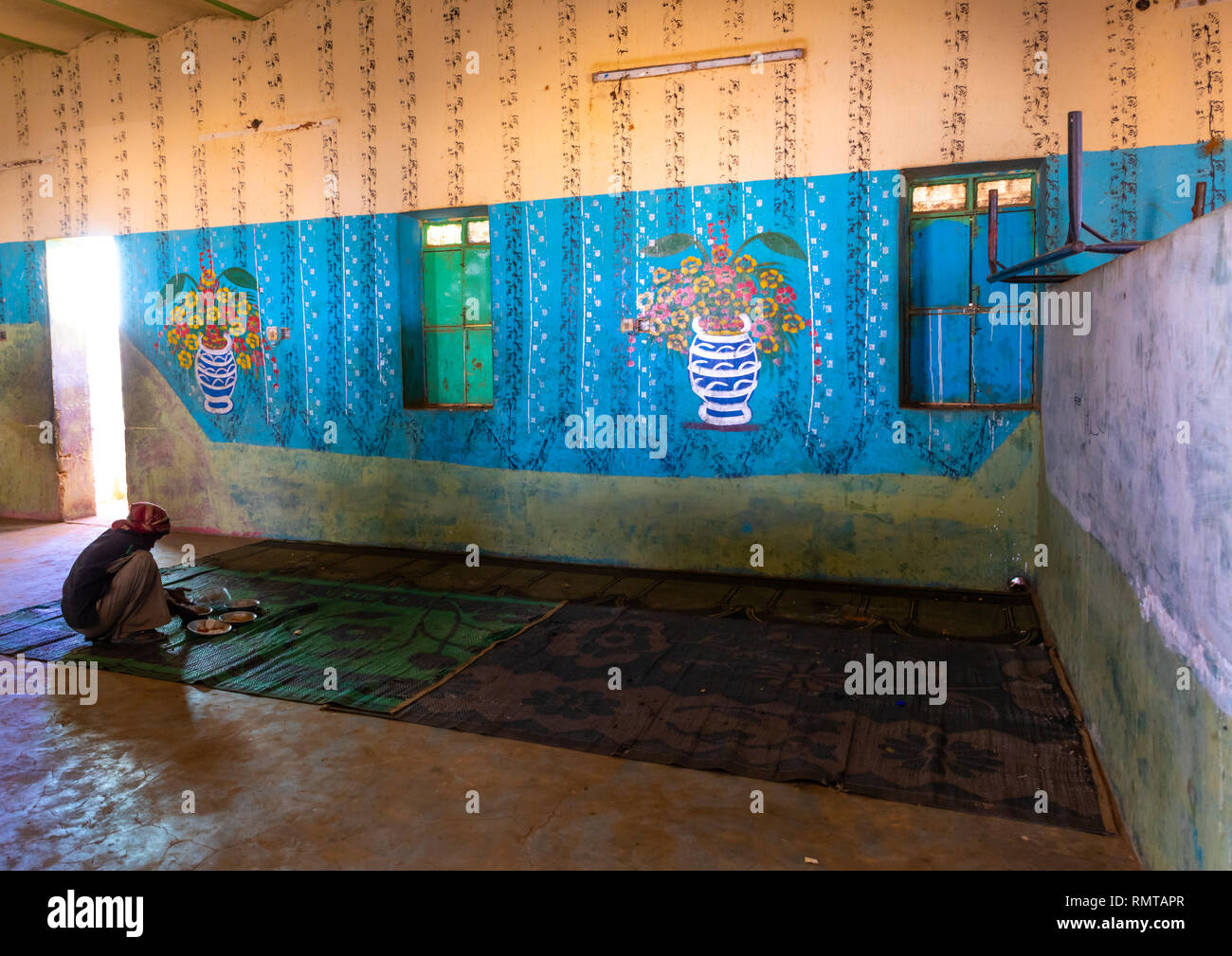 Sudanese man eating on the floor in a restaurant with decorated walls ...