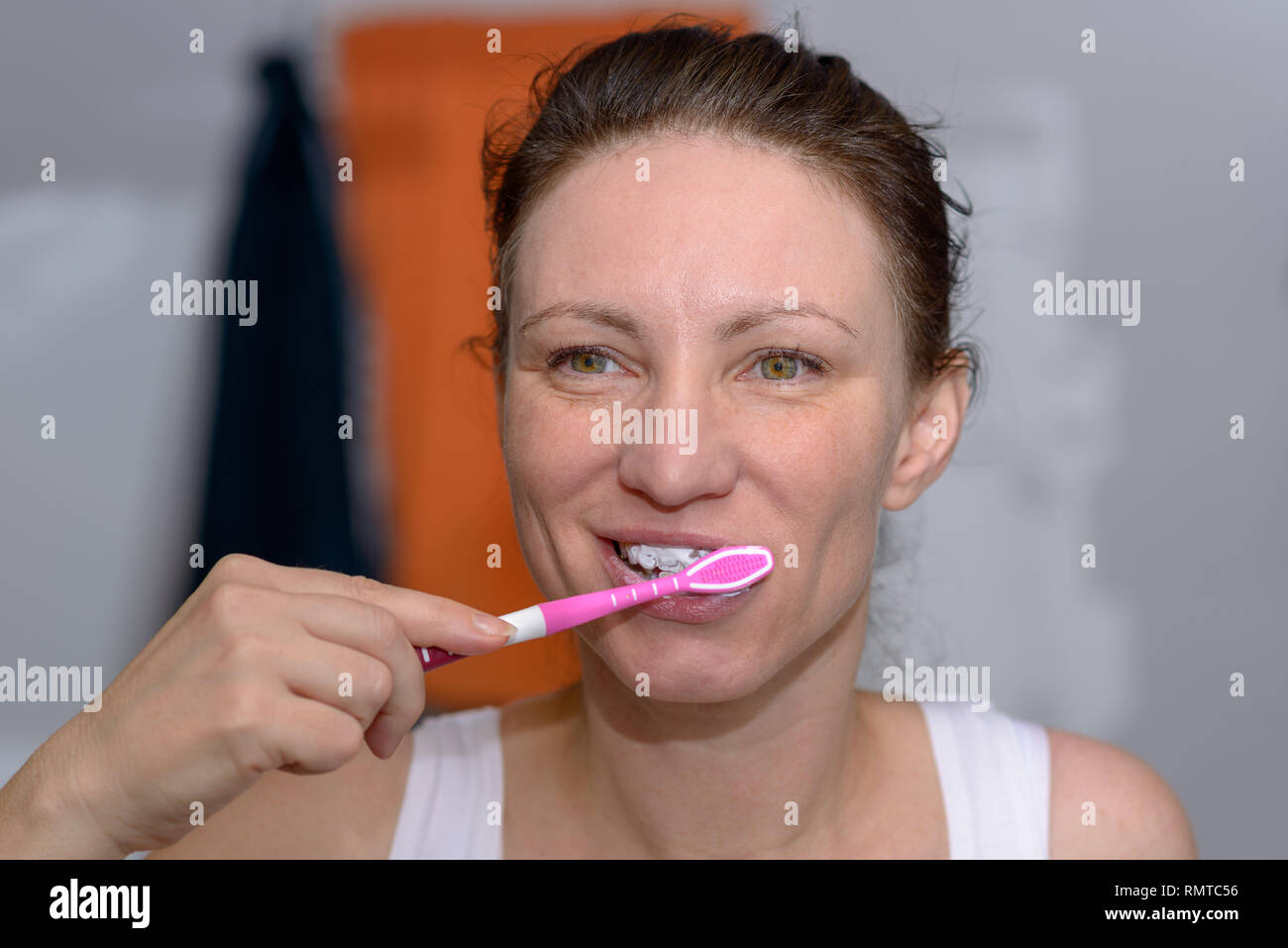 Happy woman brushing her teeth with a pink plastic toothbrush in a ...