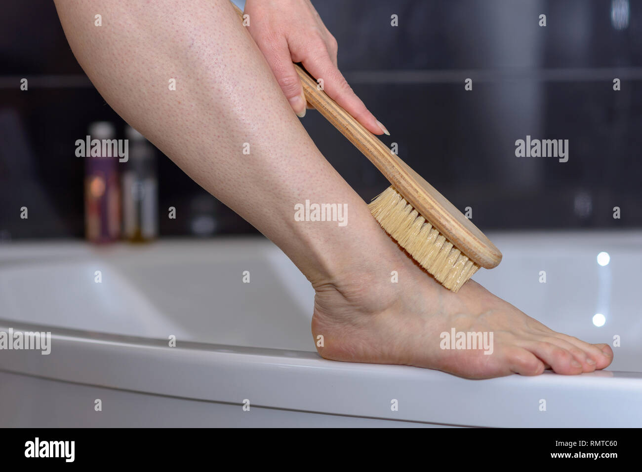 Woman scrubbing her leg with a brush balancing on the edge of a bathtub ...