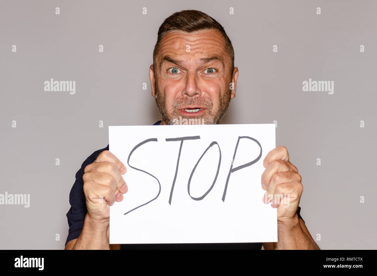 Alarmed intense middle-aged man staring wide eyed at the camera holding ...