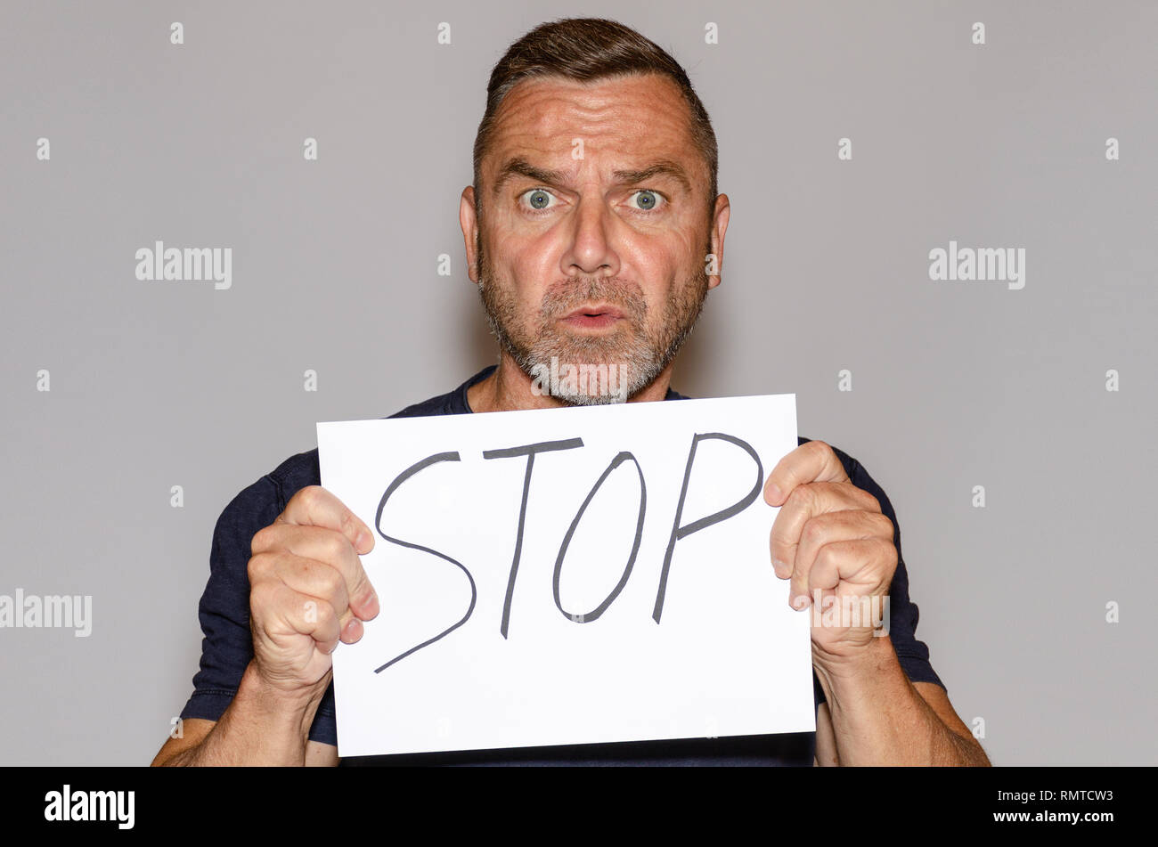 Alarmed intense middle-aged man staring wide eyed at the camera holding ...