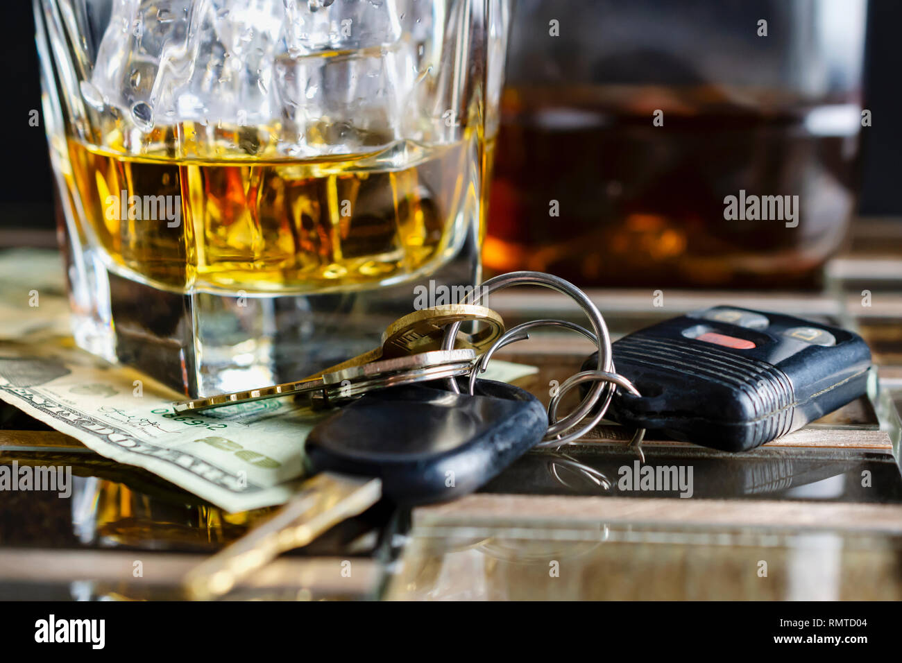 Glass of alcohol with ice, keys, and money. Close up view with nearly ...