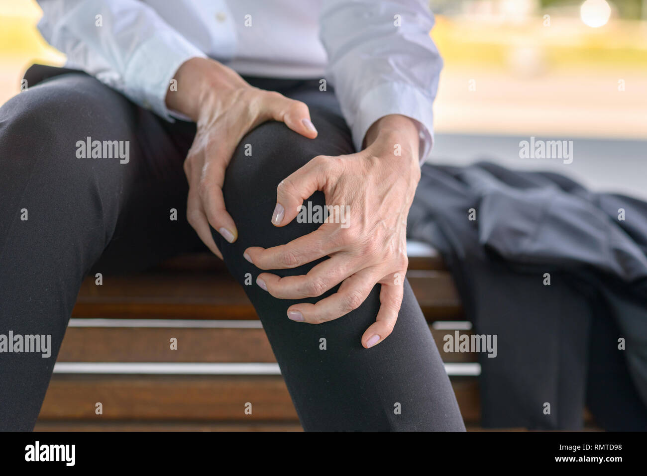 Businesswoman is holding her aching knee while sitting on a bench Stock ...