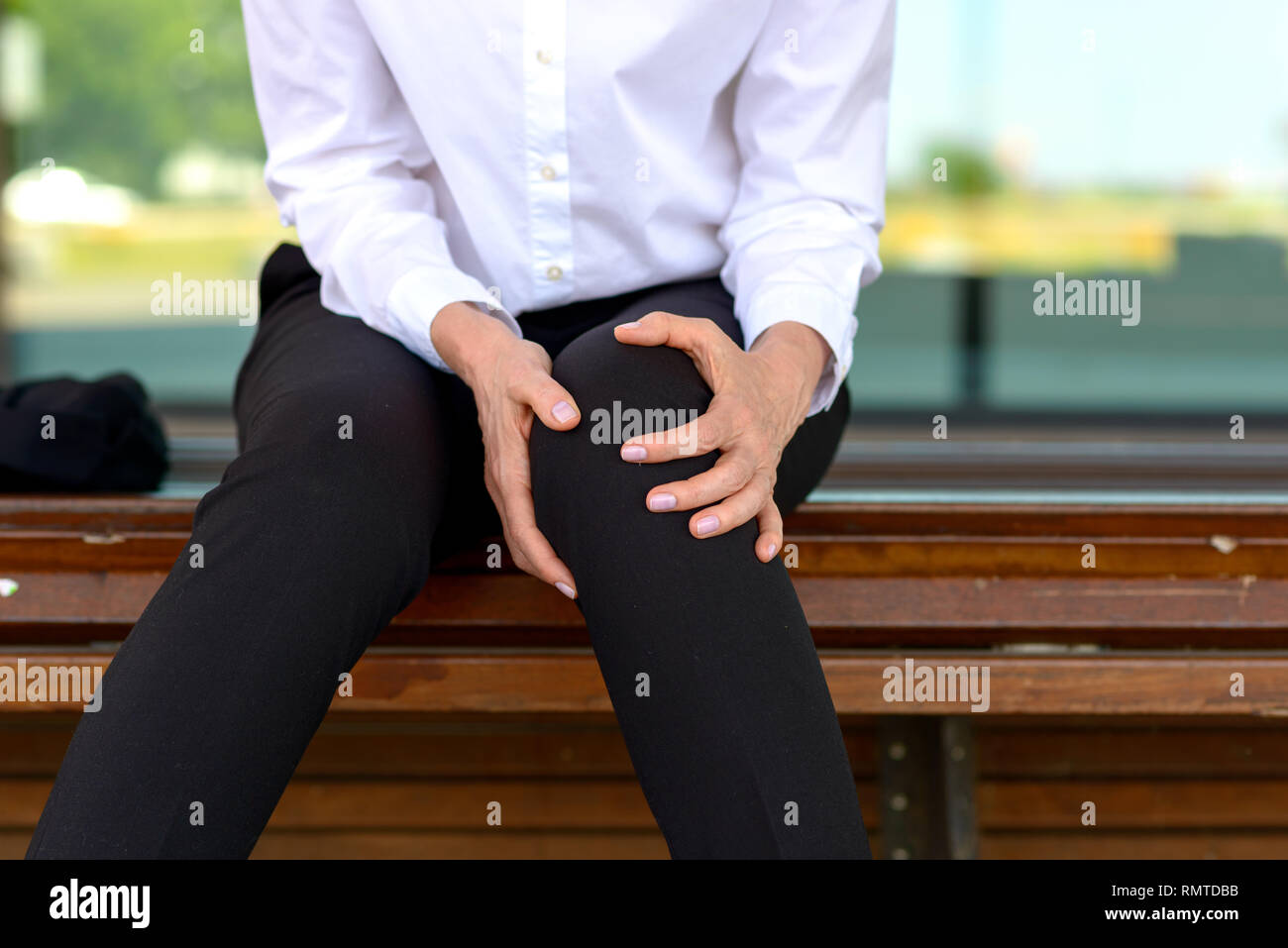 Businesswoman is holding her aching knee while sitting on a bench Stock ...