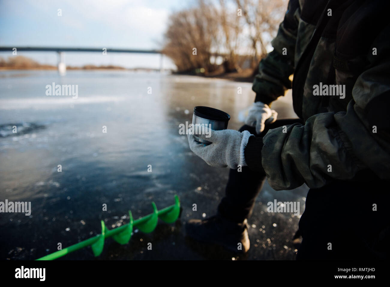 Fisherman drinking tea from a thermos in the winter on the ice. Winter ...