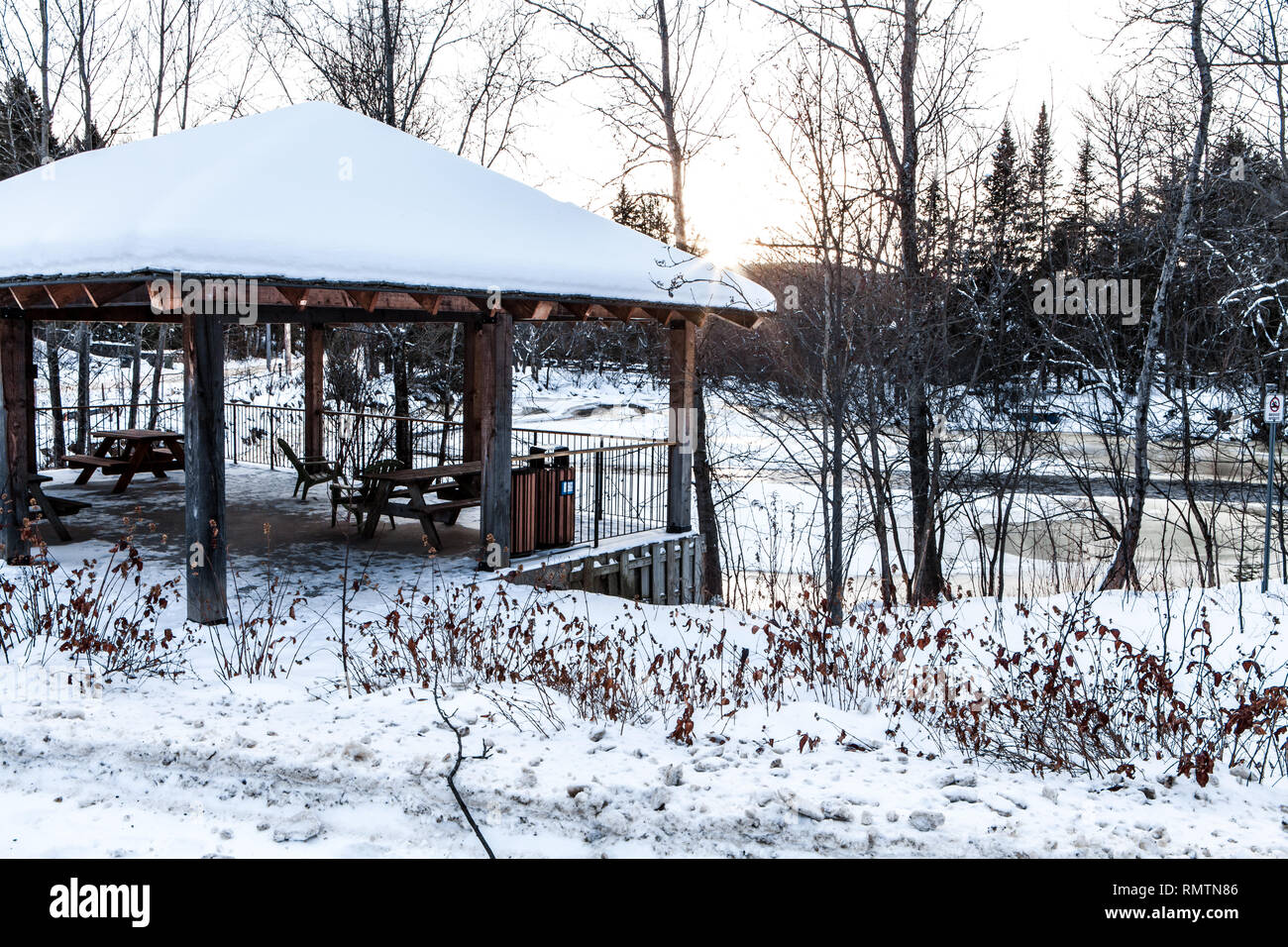 Snow covered gazebo with picnic tables, chairs and garbage bins on the ...