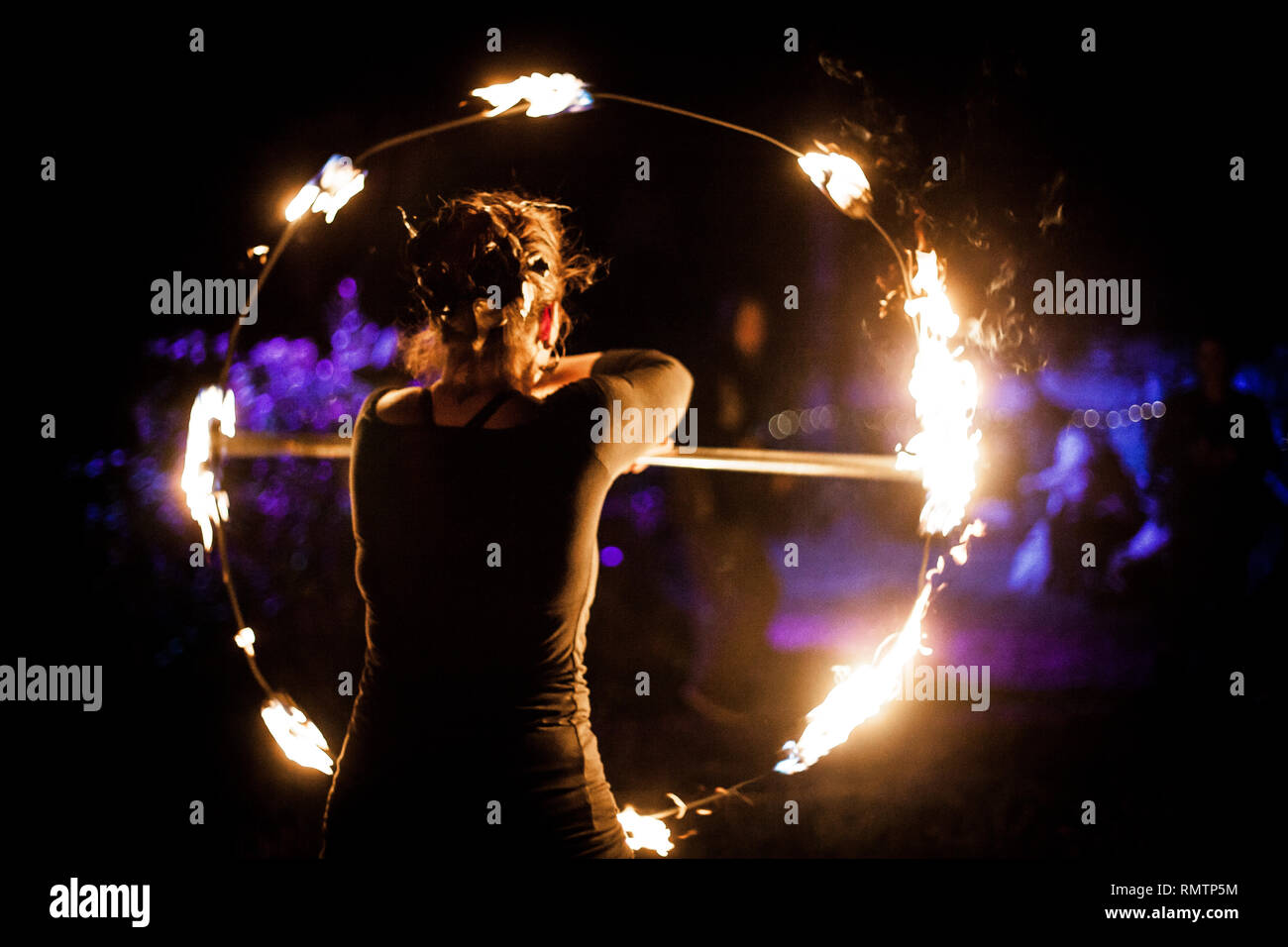 Woman spinning fire at night, in front of an audience, seen from behind ...