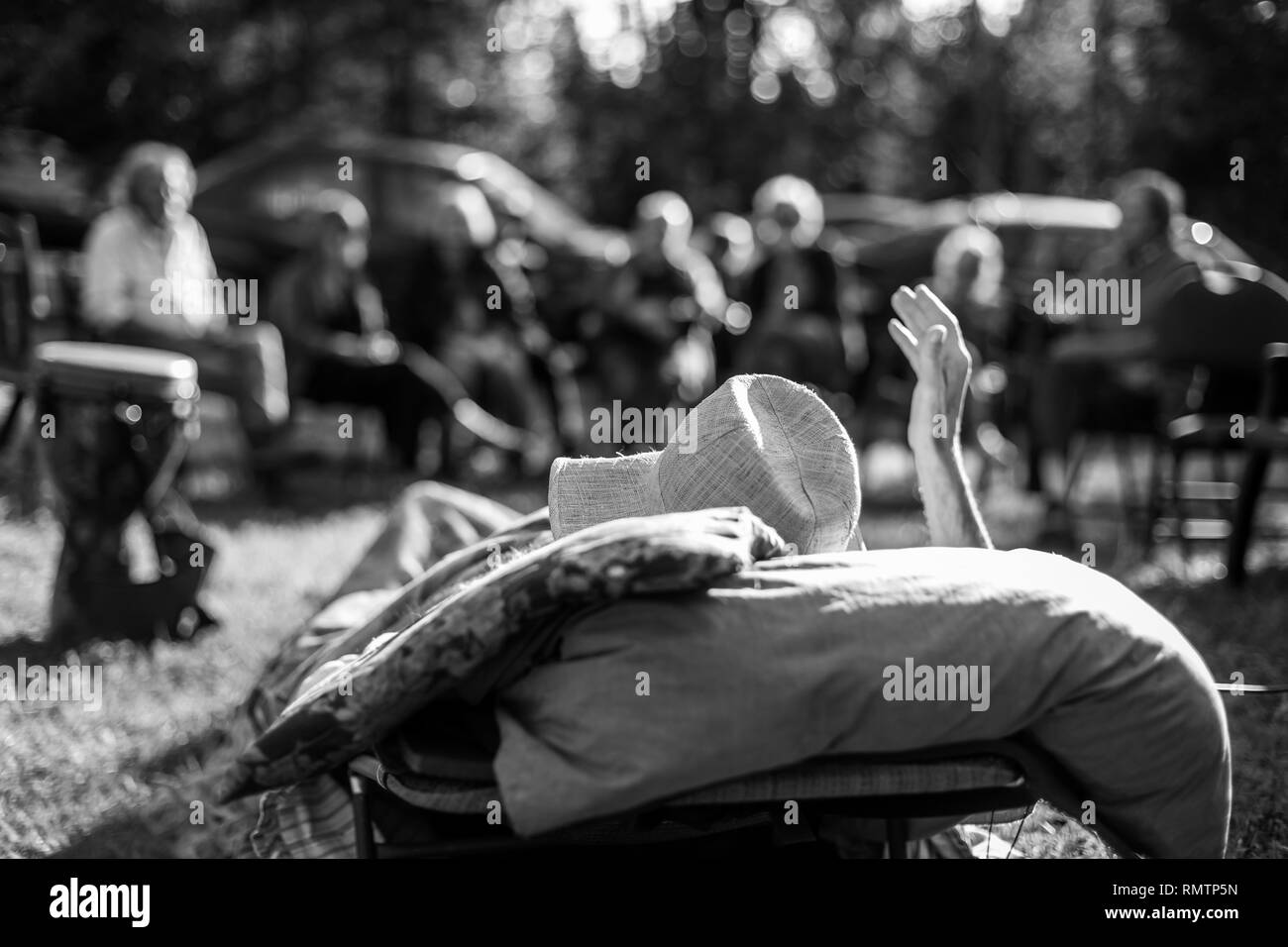 Old man lying in a bed on the grass talking to an audience, seen from ...