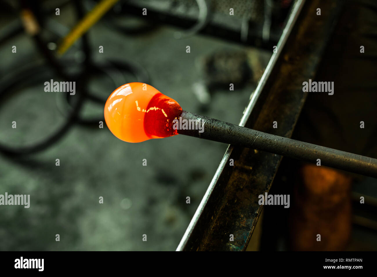 Glass-blower man working with hot orange glass to make a blown glass ...