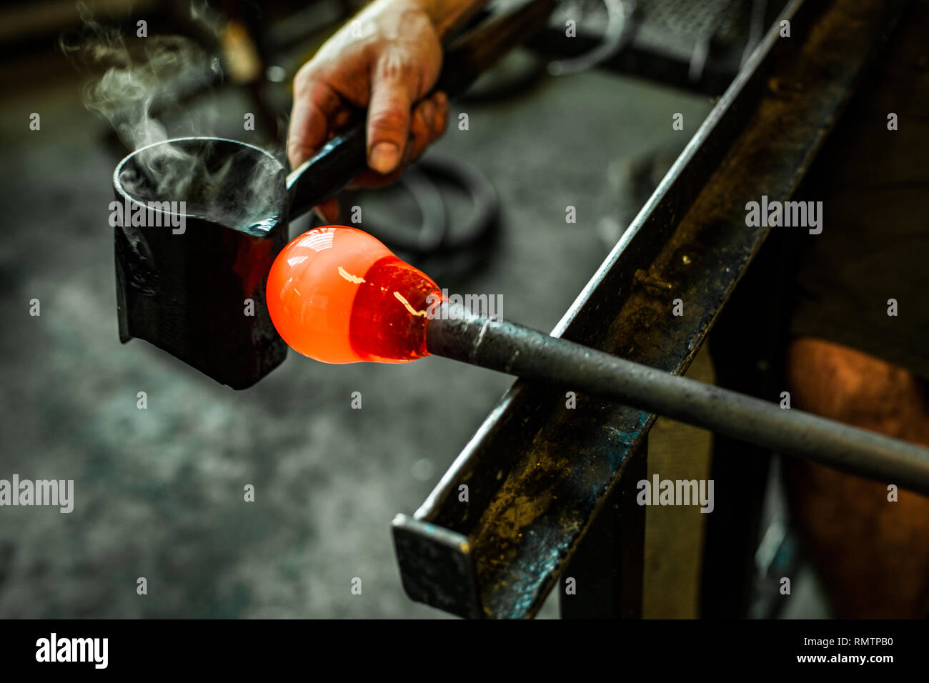 Glass-blower man working with hot orange glass to make a blown glass ...