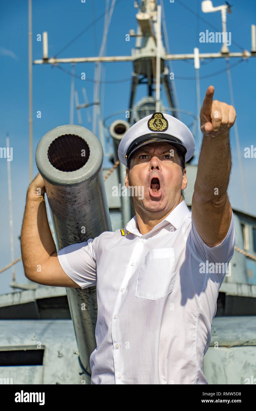 A navy officer standing beside gun and pointing his finger ahead.The ...