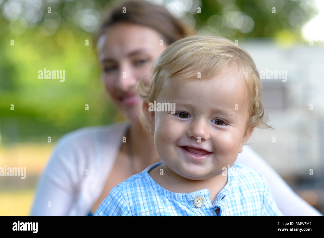 Happy smiling blond baby boy outdoors in a close up head and shoulders ...