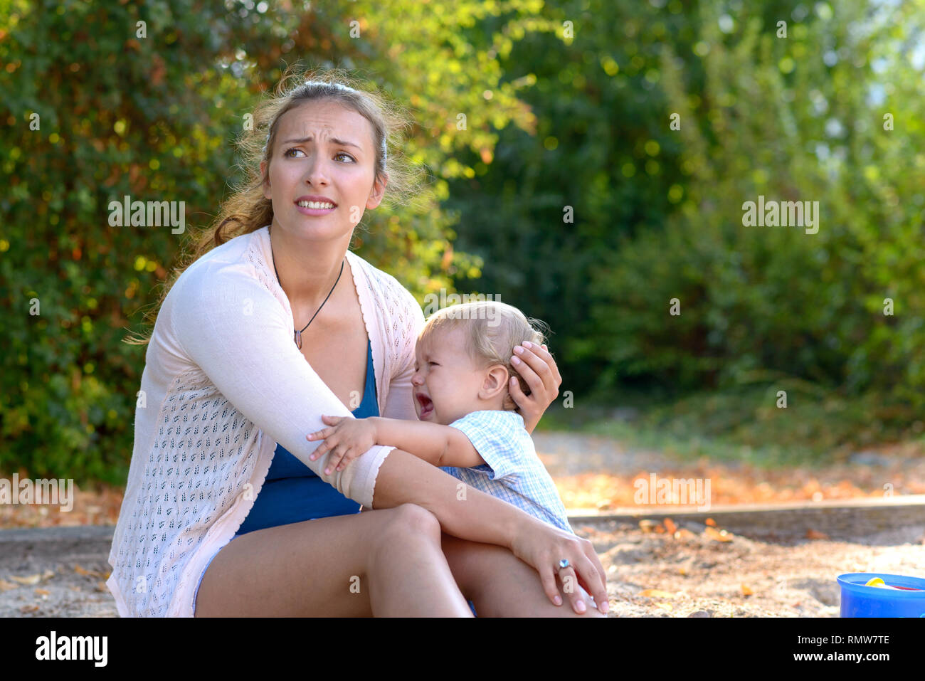 Stressed young mother comforting her crying baby son looking away with ...