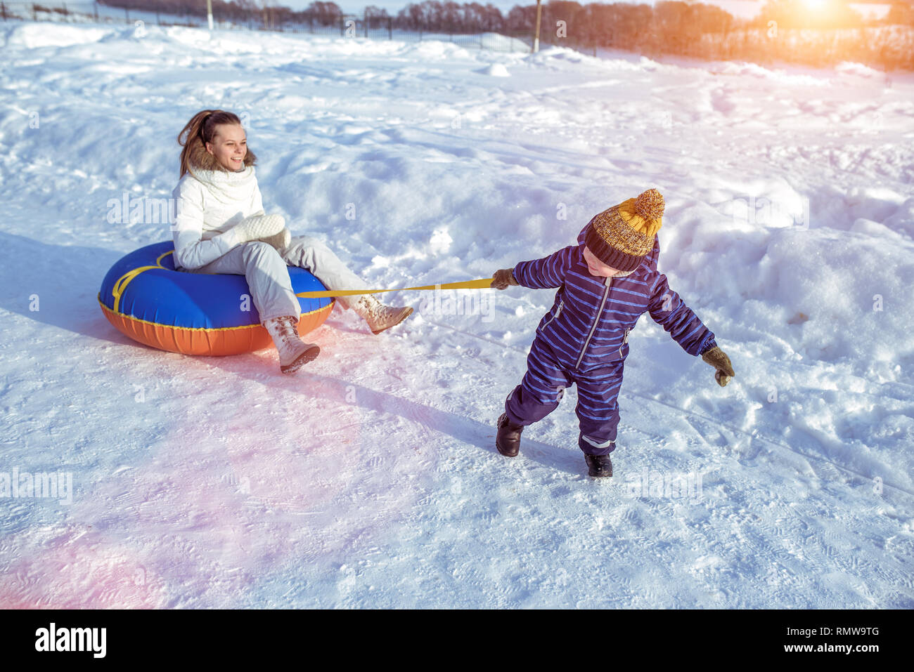 A little boy is dragging a tubing sling on rope on which the mother is ...