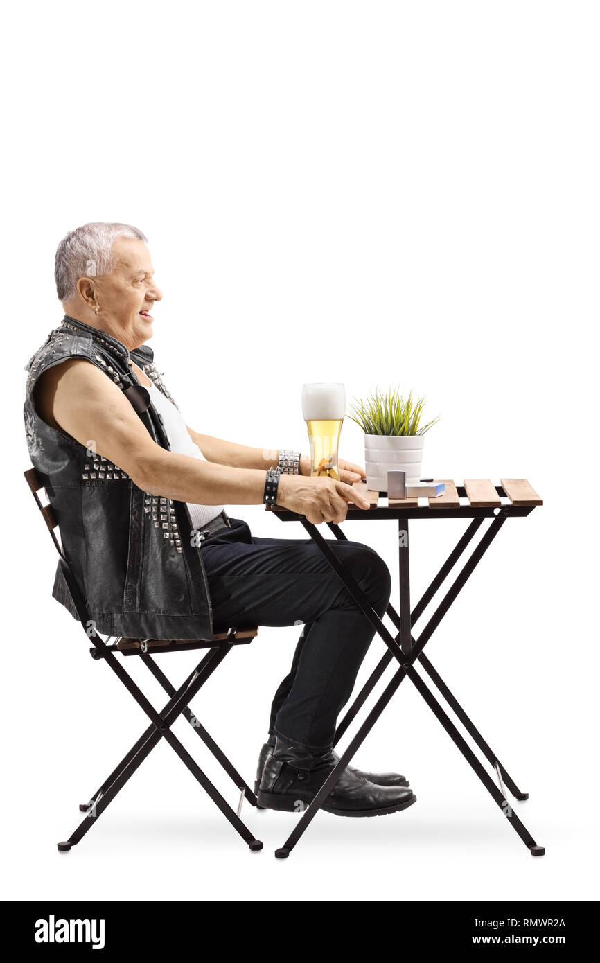 Full length profile shot of an old punk man sitting at a table and ...