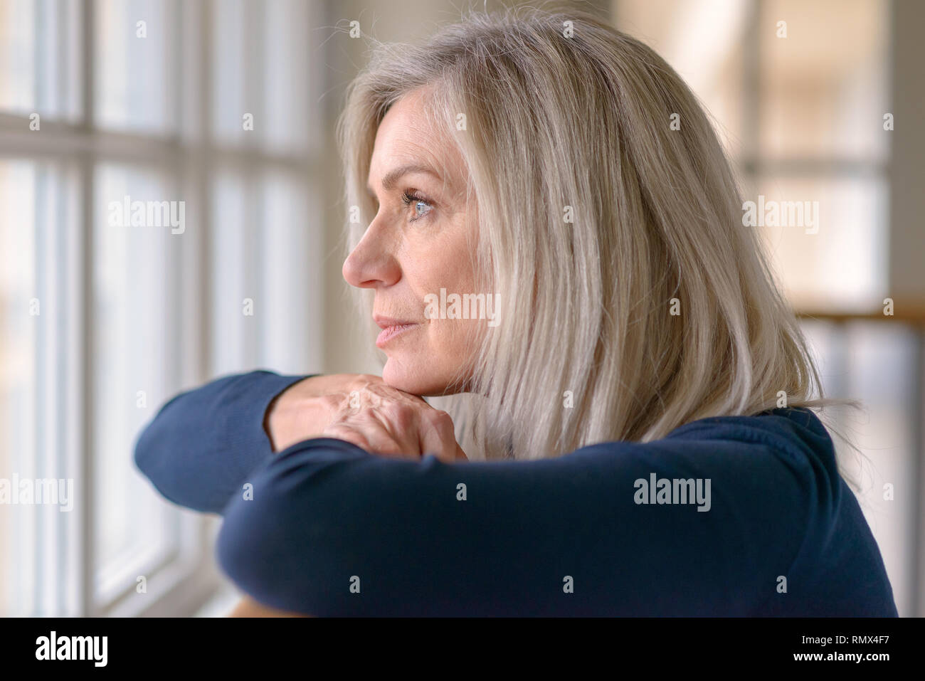 Attractive blond woman watching through a window with a serious ...