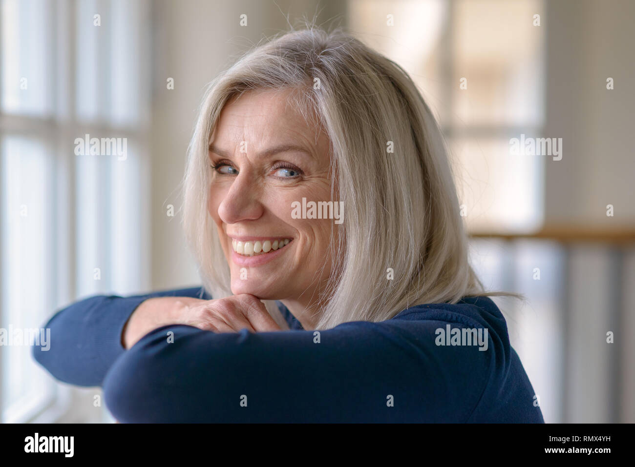 Happy blond woman with a vivacious friendly smile turning to glance at ...