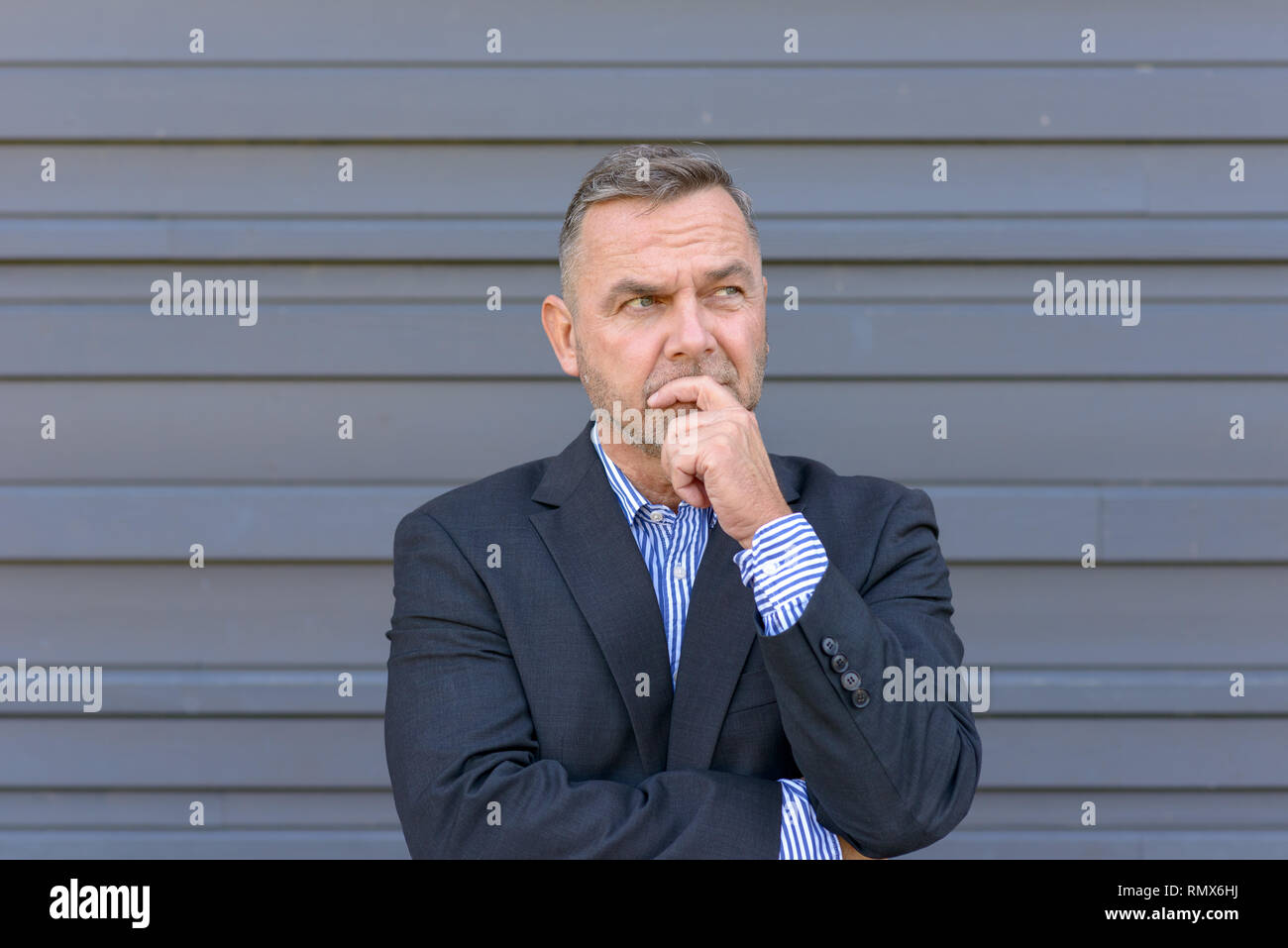 Smart middle-aged man standing thinking with his hand to his chin ...