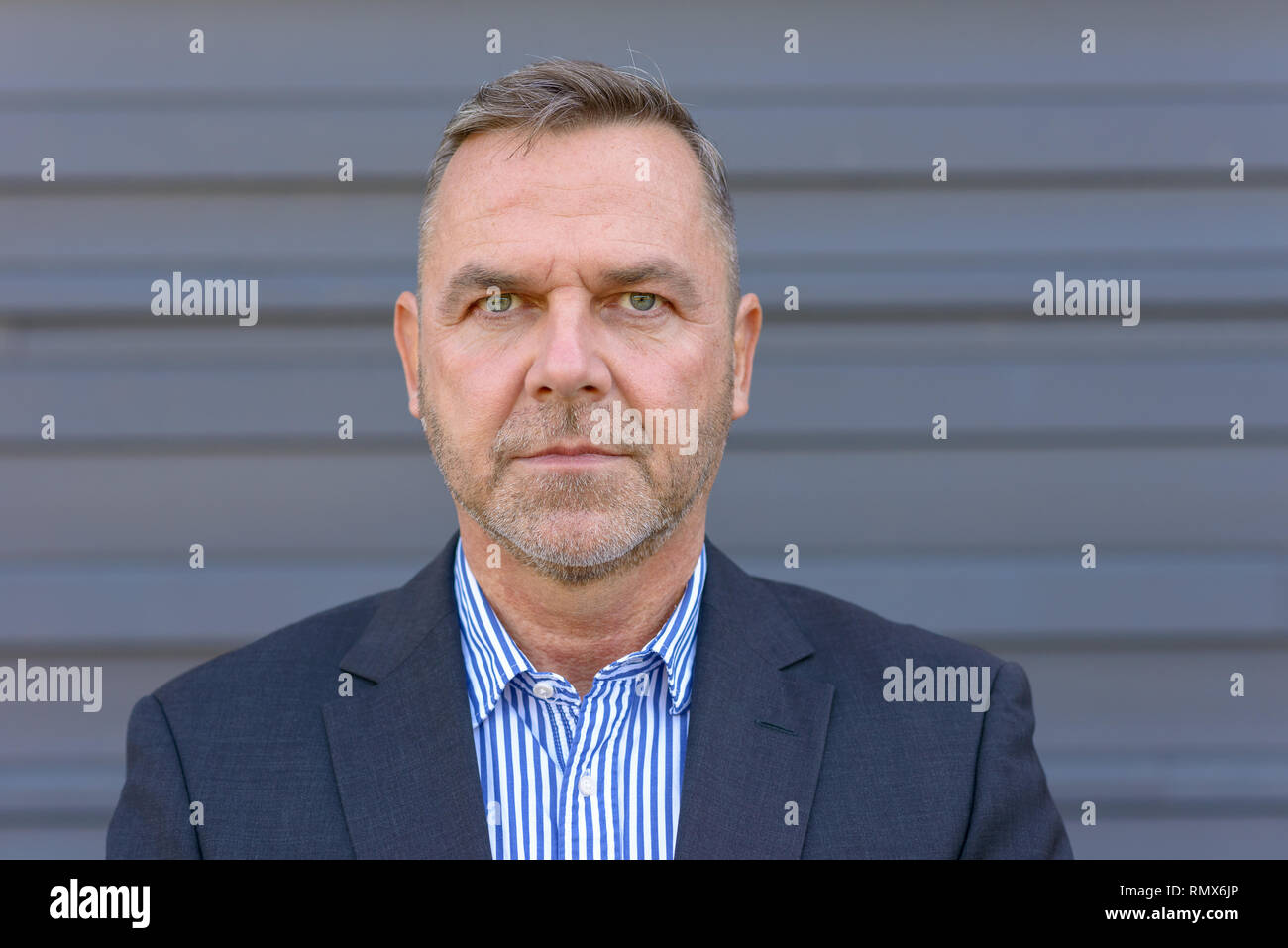 Serious businessman with an inscrutable expression standing against a ...