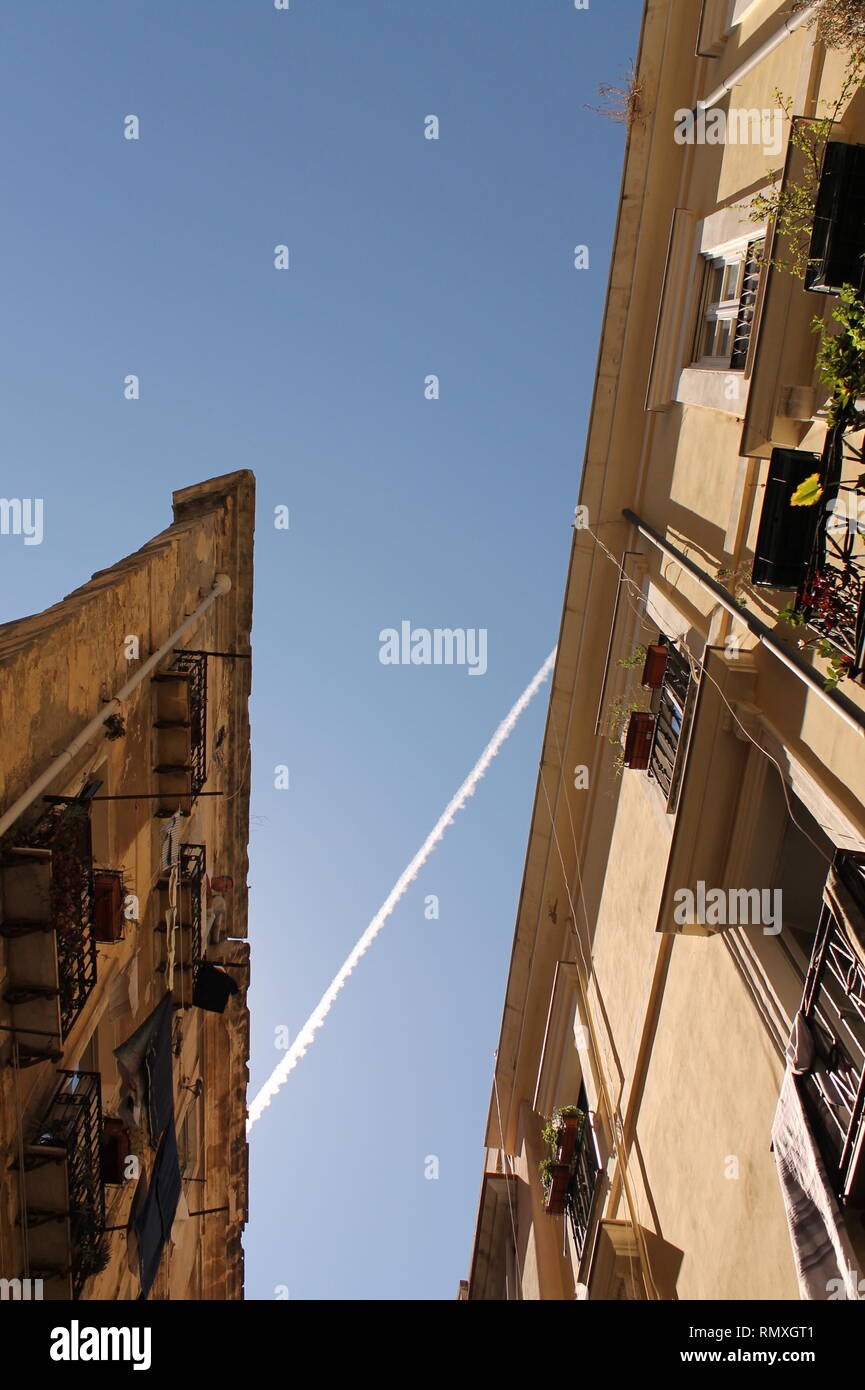 A plane line on the blue sky between buildings Stock Photo - Alamy