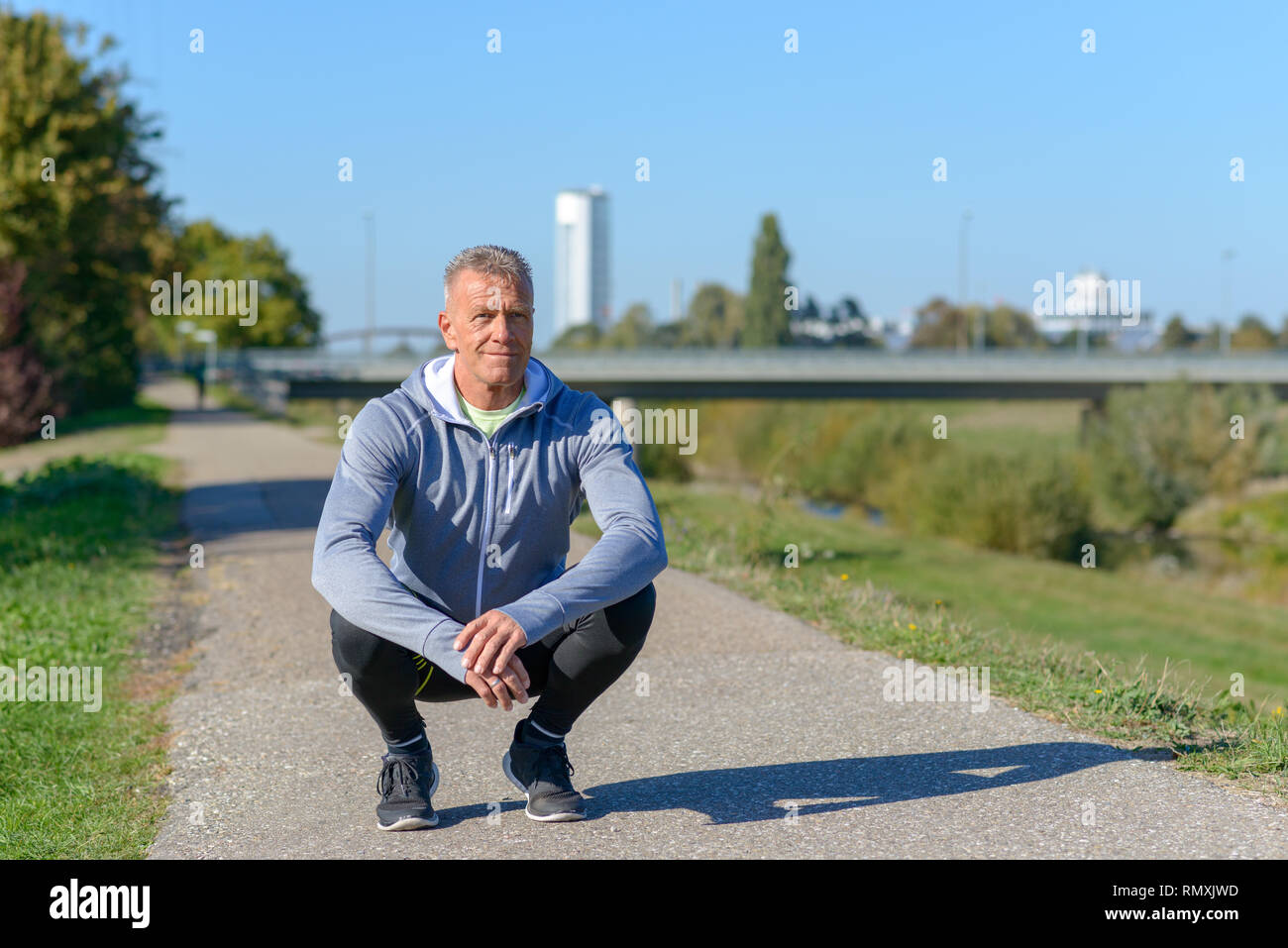 Smiling middle aged runner sitting in a squat while taking a break ...