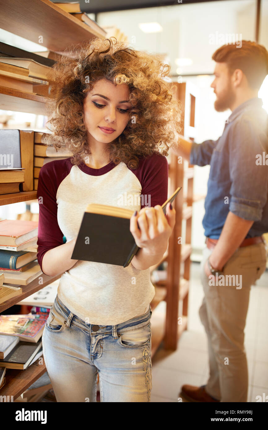 Curly young girl in library read book Stock Photo - Alamy