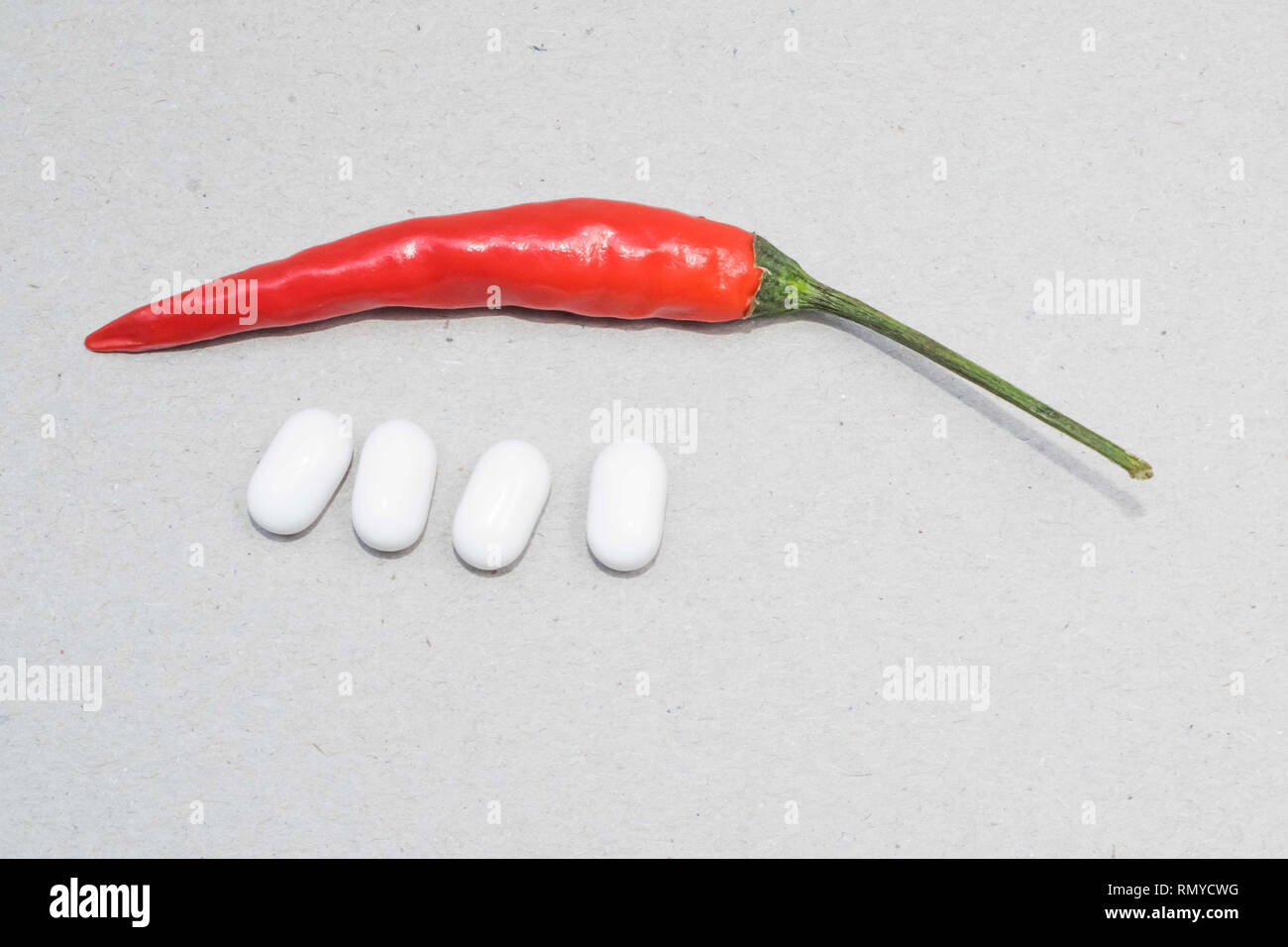 Single red chilli pepper and four white capsules on a white background ...