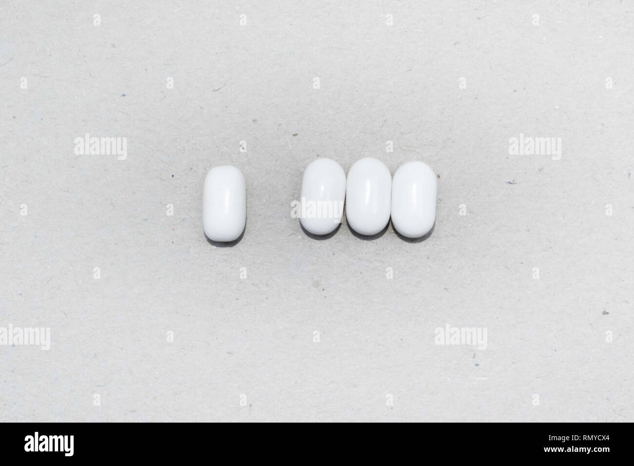 Three white capsules on a white background and a single capsule aside ...