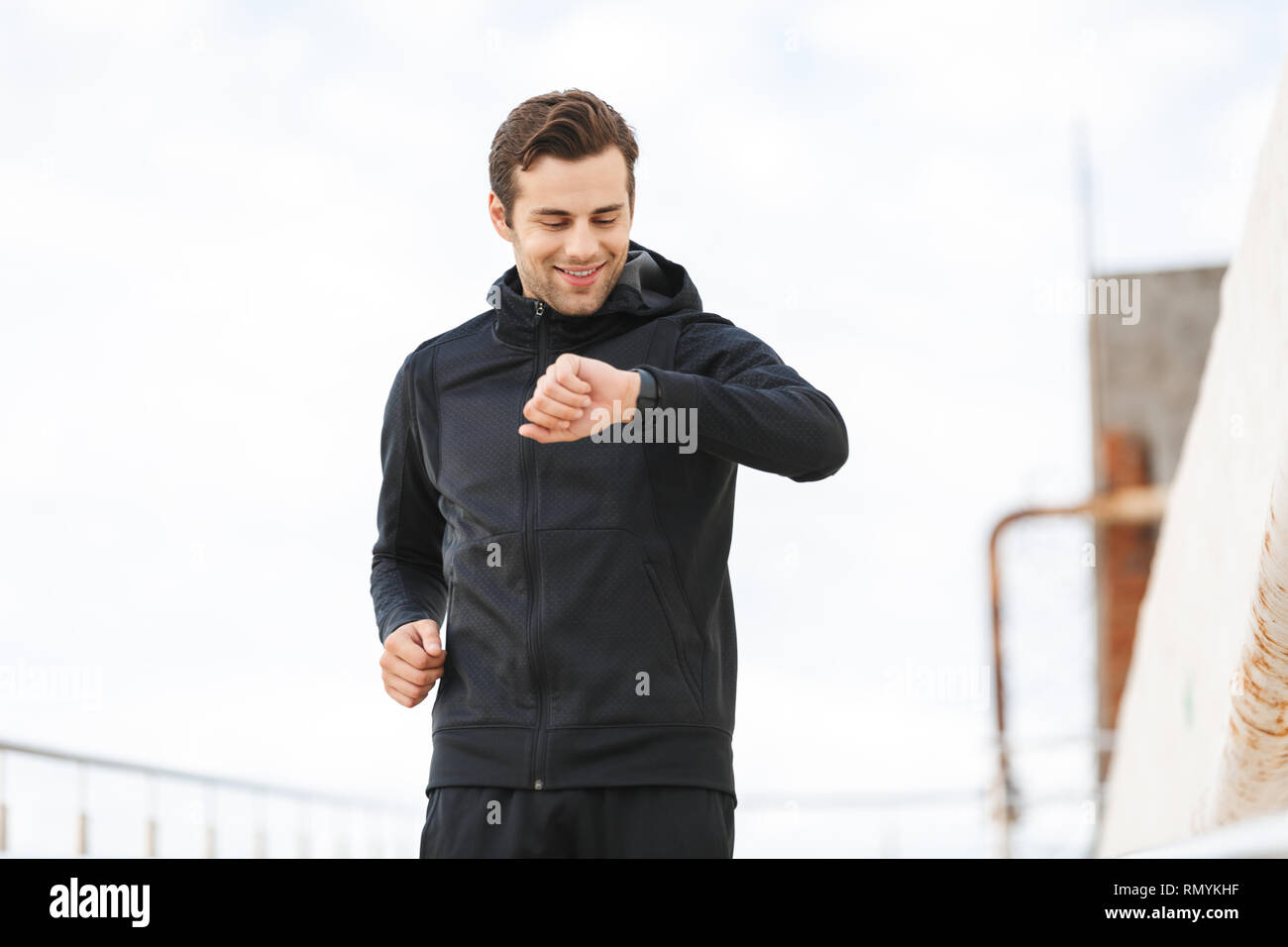 Image of muscular sporty man 30s in black sportswear running along pier ...