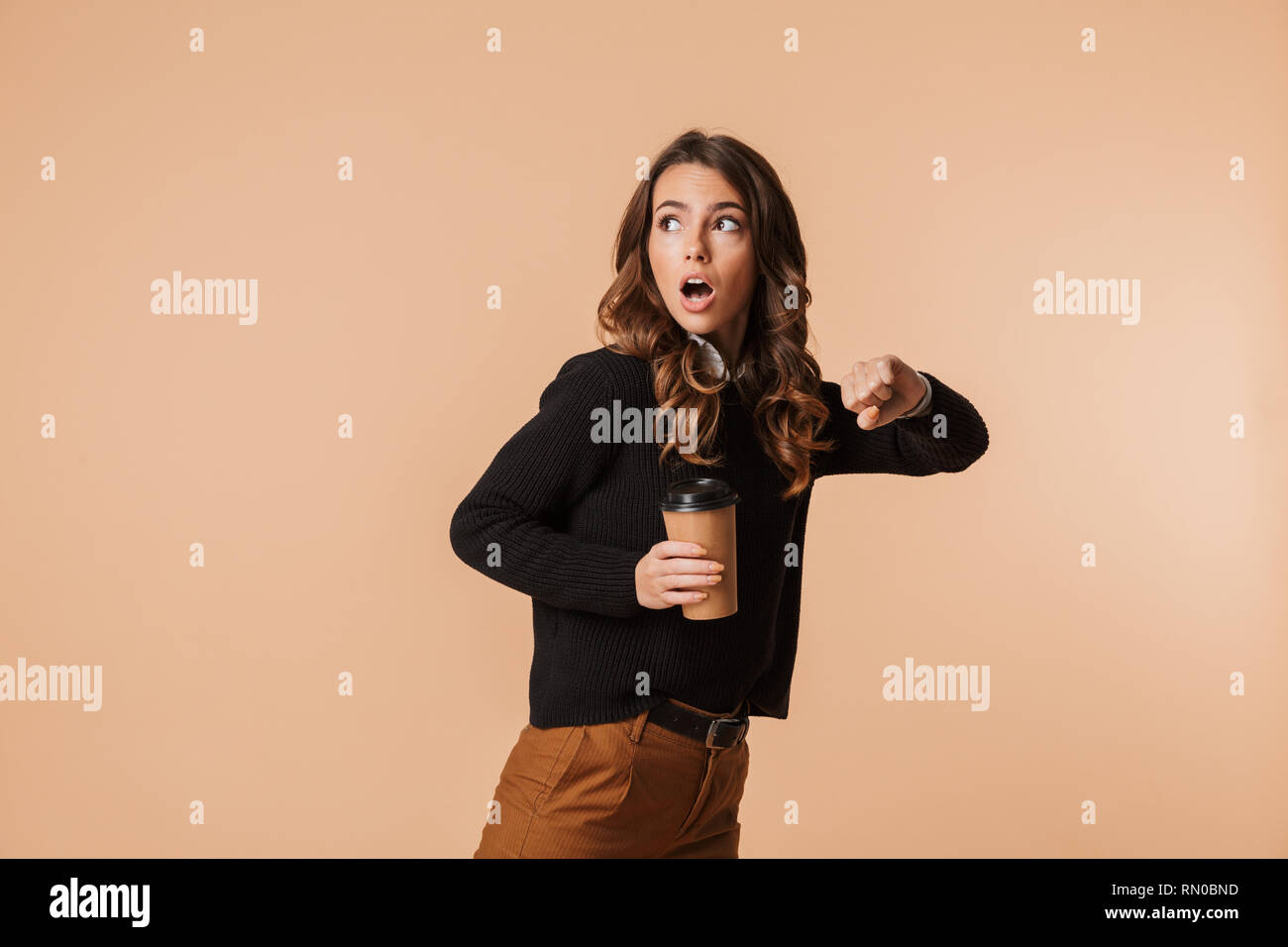 Shocked young woman wearing sweater running late isolated over beige ...