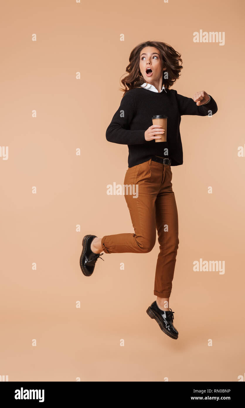 Shocked young woman wearing sweater running late isolated over beige ...