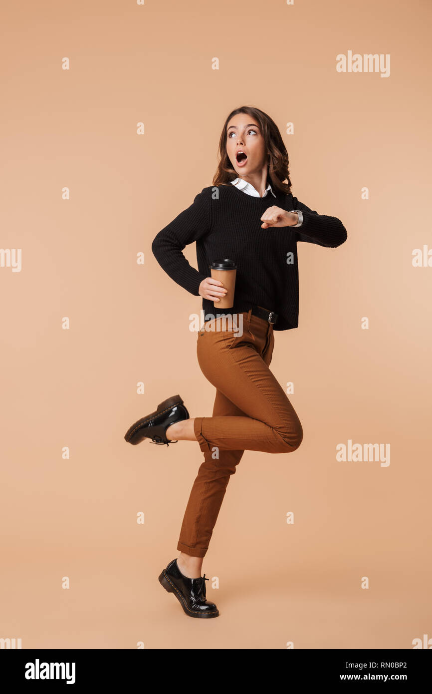 Shocked young woman wearing sweater running late isolated over beige ...