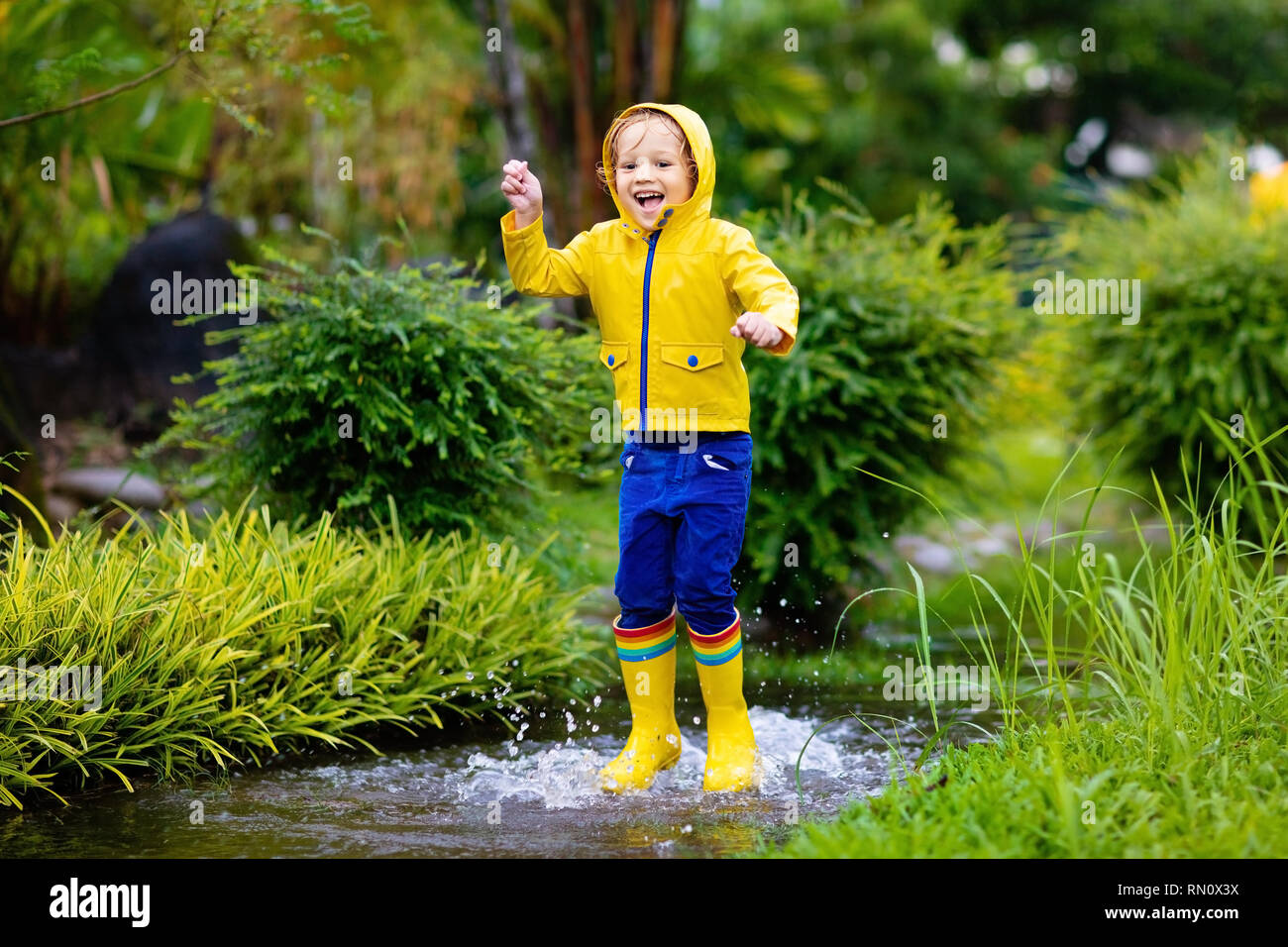Kid playing in the rain in autumn park. Child jumping in muddy puddle ...
