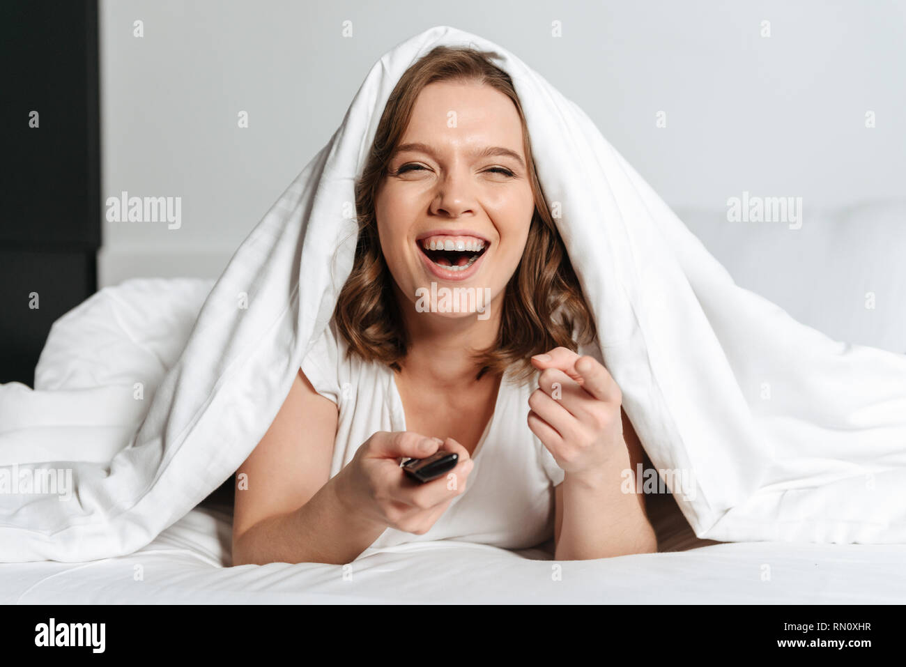 Attractive Young Woman Lying In Bed At Home Watching Tv Laughing Stock