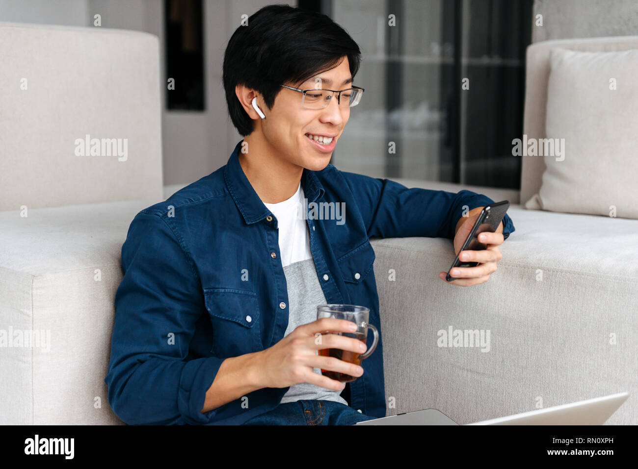 Happy asian man sitting on a couch at home, using laptop computer ...