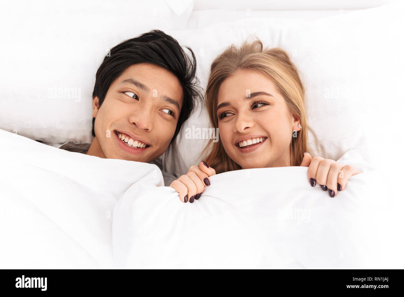 Happy young couple laying in bed Stock Photo - Alamy
