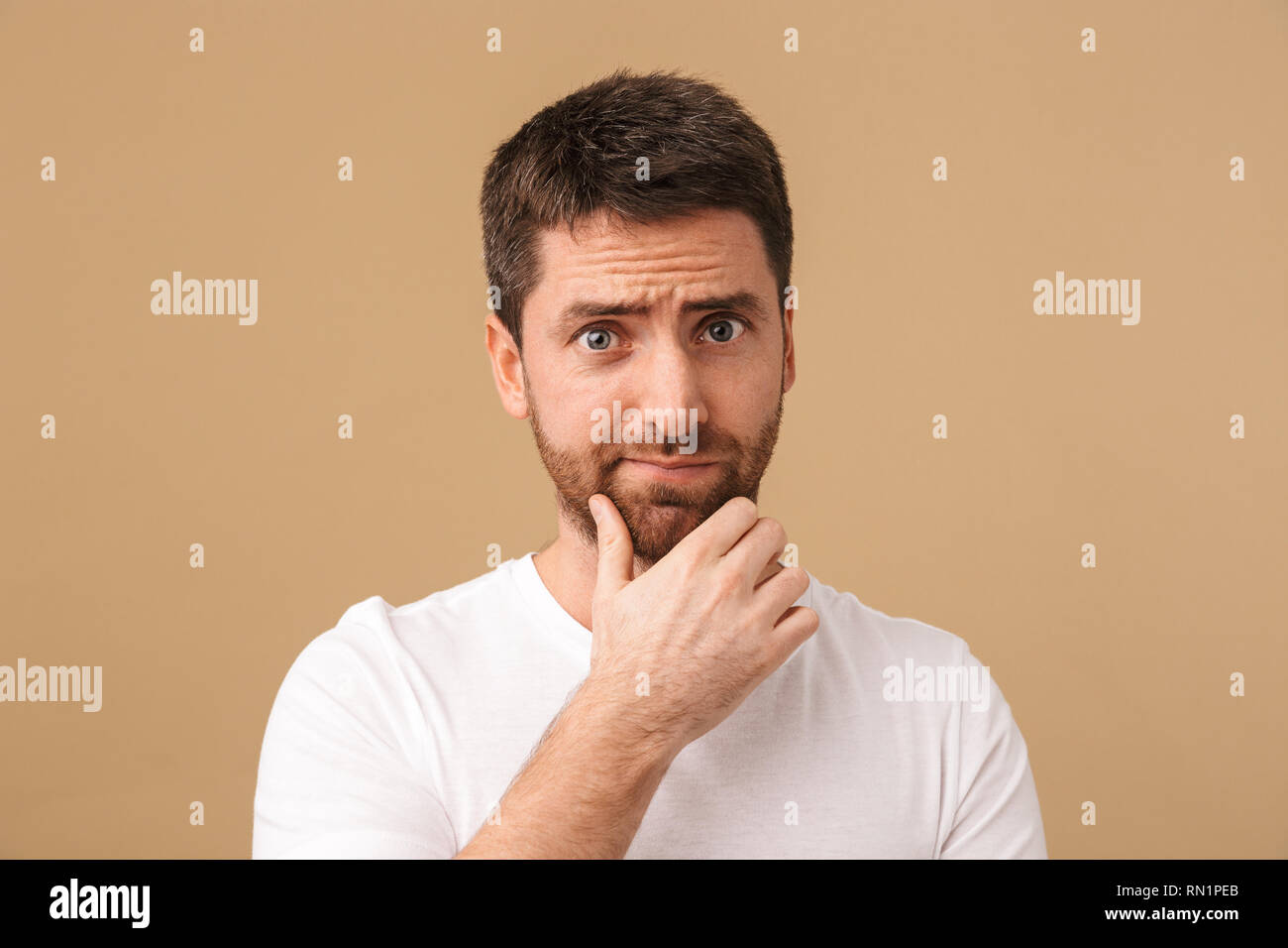 Portrait of a confused young man casually dressed standing isolated ...