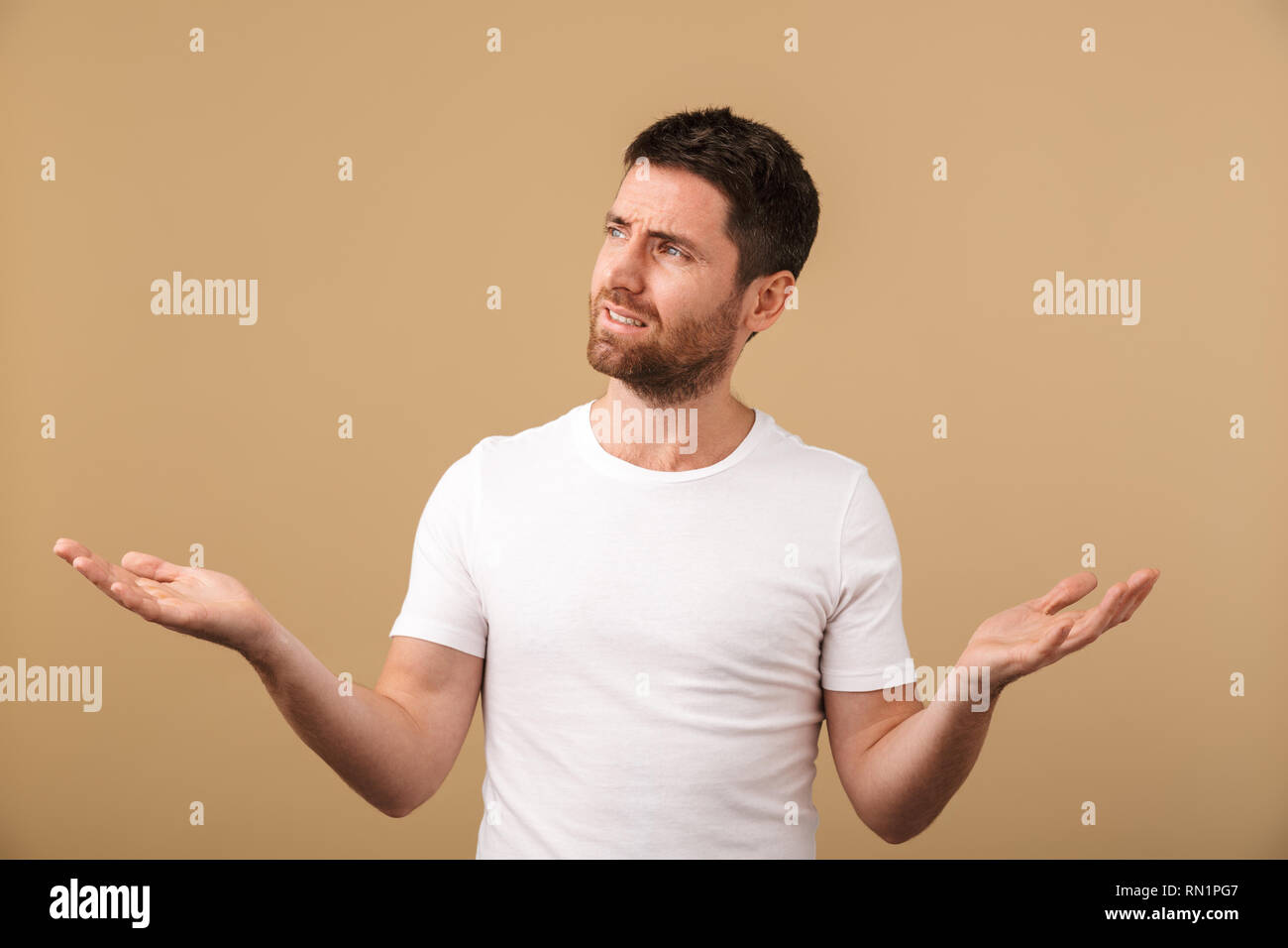 Portrait of a confused young man casually dressed standing isolated ...